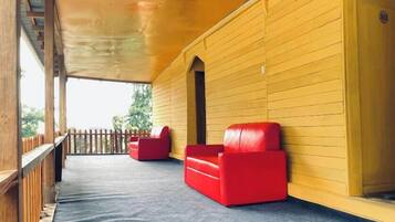 Um espaço coberto ao ar livre com paredes de madeira, um sofá vermelho e uma pequena mesa.