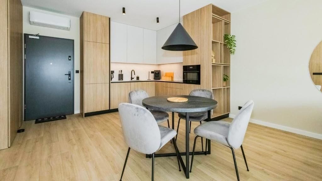 Uma cozinha moderna com uma mesa de jantar redonda e quatro cadeiras, uma luminária pendente preta e armários embutidos de madeira.