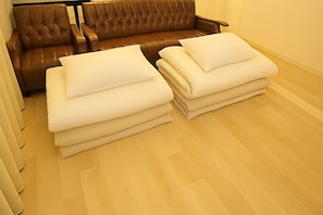 Um quarto com um sofá de couro marrom e duas pilhas de almofadas brancas sobre um piso de madeira.