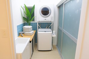 Uma lavanderia compacta com máquina de lavar, varal sobreposto, secador de cabelo e uma planta.