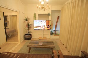 Uma sala de estar com televisão, mesa de madeira, planta em vaso e um candelabro.