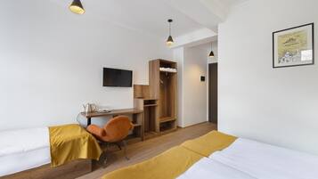 Quarto de hotel com duas camas de solteiro, uma escrivaninha, uma cadeira, uma televisão e um guarda-roupa de madeira.