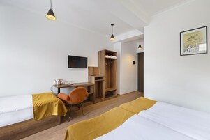 Quarto de hotel com duas camas de solteiro, uma escrivaninha, uma cadeira, uma televisão e um guarda-roupa de madeira.