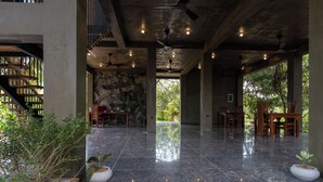 Um espaço amplo e interno, com piso lustroso, escada e área de estar com mesas e cadeiras.