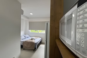 Um quarto com uma cama, uma janela e um micro-ondas.