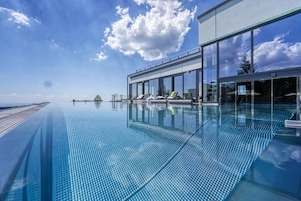 Um edifício moderno com fachada de vidro, área de piscina com espreguiçadeiras e céu claro.