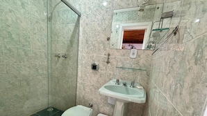 Uma casa de banho com sanita, cabine de duche em vidro, lavatório e espelho.