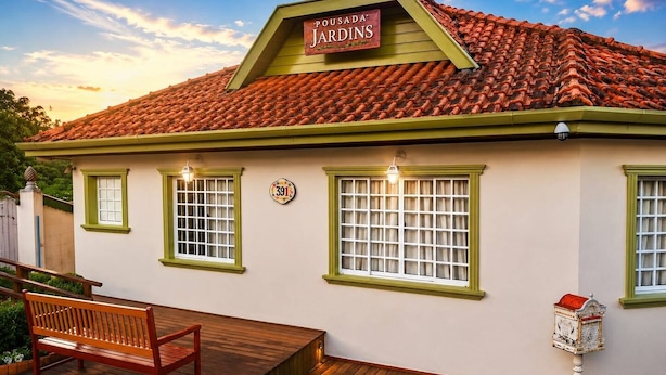 Um edifício com uma placa indicando 'POUSADA JARDINS', um banco de madeira e uma caixa de correio.
