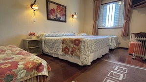 Quarto de hotel com duas camas, uma mesa de cabeceira, um radiador e uma janela com cortinas.
