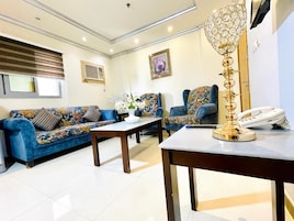 Uma sala de estar com um sofá, duas poltronas, uma mesa de centro, um abajur decorativo e um telefone.
