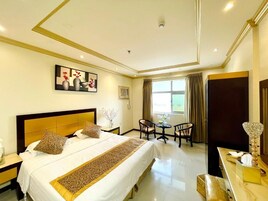 Quarto de hotel com cama, escrivaninha, cadeira, janela com cortinas e um quadro na parede.