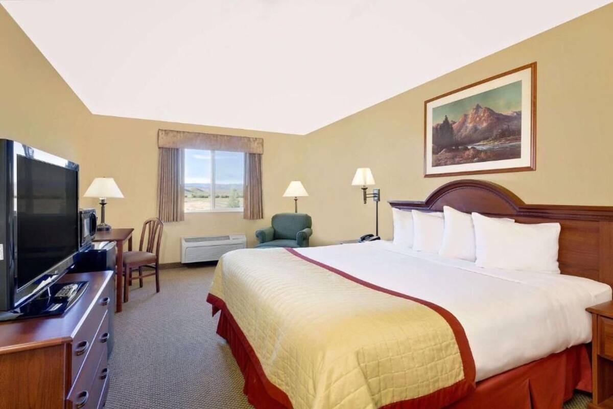 Quarto de hotel com uma cama grande, televisão, escrivaninha e cadeira.