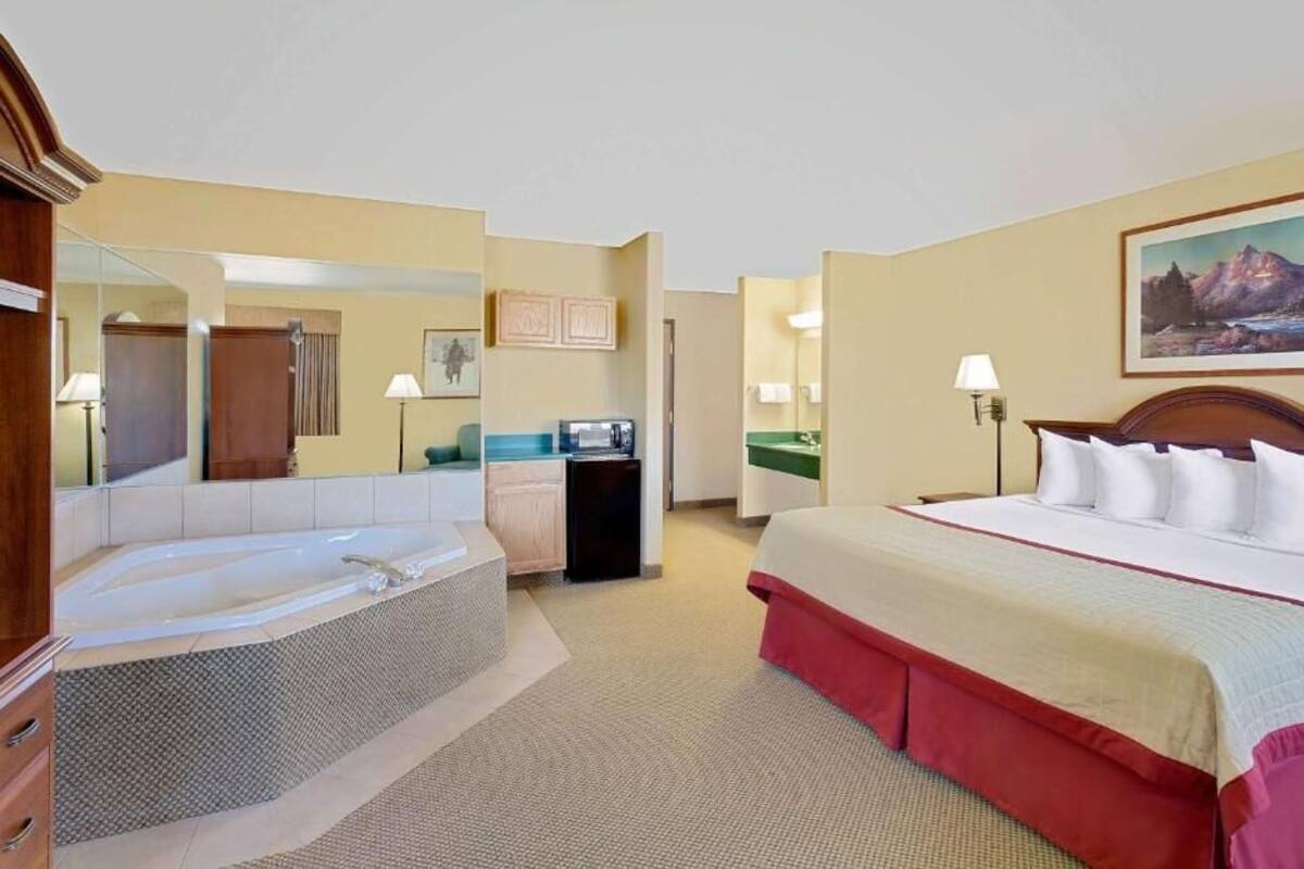 Quarto de hotel com uma cama grande, banheiro privativo com banheira, escrivaninha e um quadro na parede.