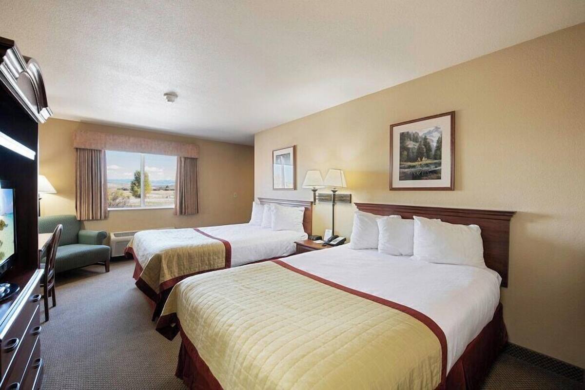 Quarto de hotel com duas camas, uma mesa de trabalho com televisão, uma cadeira e uma janela com vista.