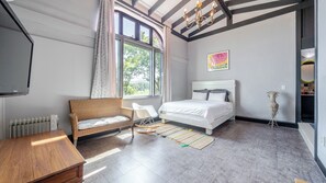 Quarto com cama, sofá, televisão e janela com cortinas.