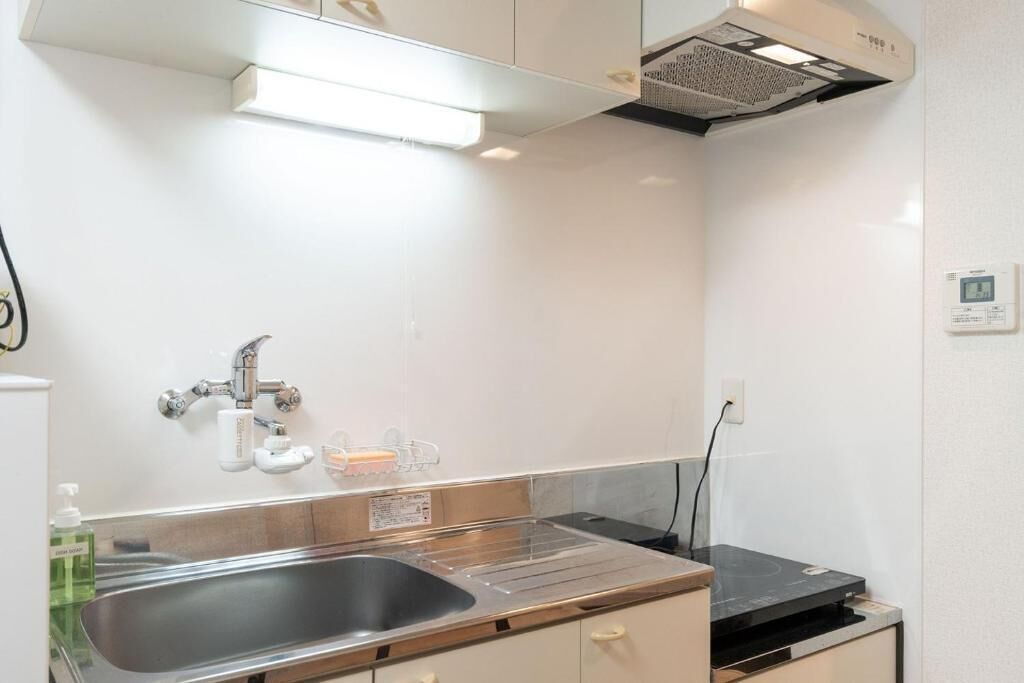 Cozinha com pia de aço inoxidável, coifa e termostato fixado na parede.