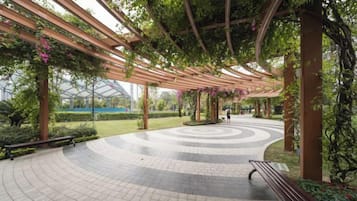 Uma galeria coberta com bancos, rodeada por vegetação e um pavimento ornamental.