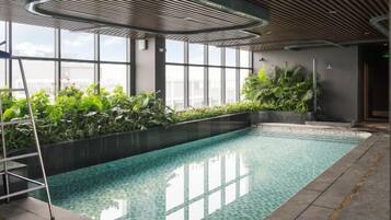 Piscina interna com vista para a cidade, cercada por plantas e com uma escada à esquerda.