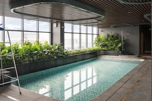 Piscina interna com vista para a cidade, cercada por plantas e com uma escada à esquerda.
