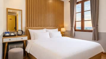 Quarto de hotel com cama, mesa de cabeceira, luminária e janela com cortinas.