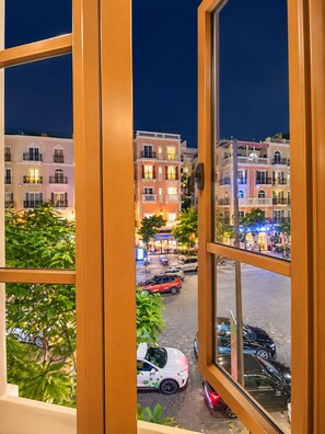 Vista da janela sobre uma rua com carros estacionados e edifícios com janelas iluminadas.