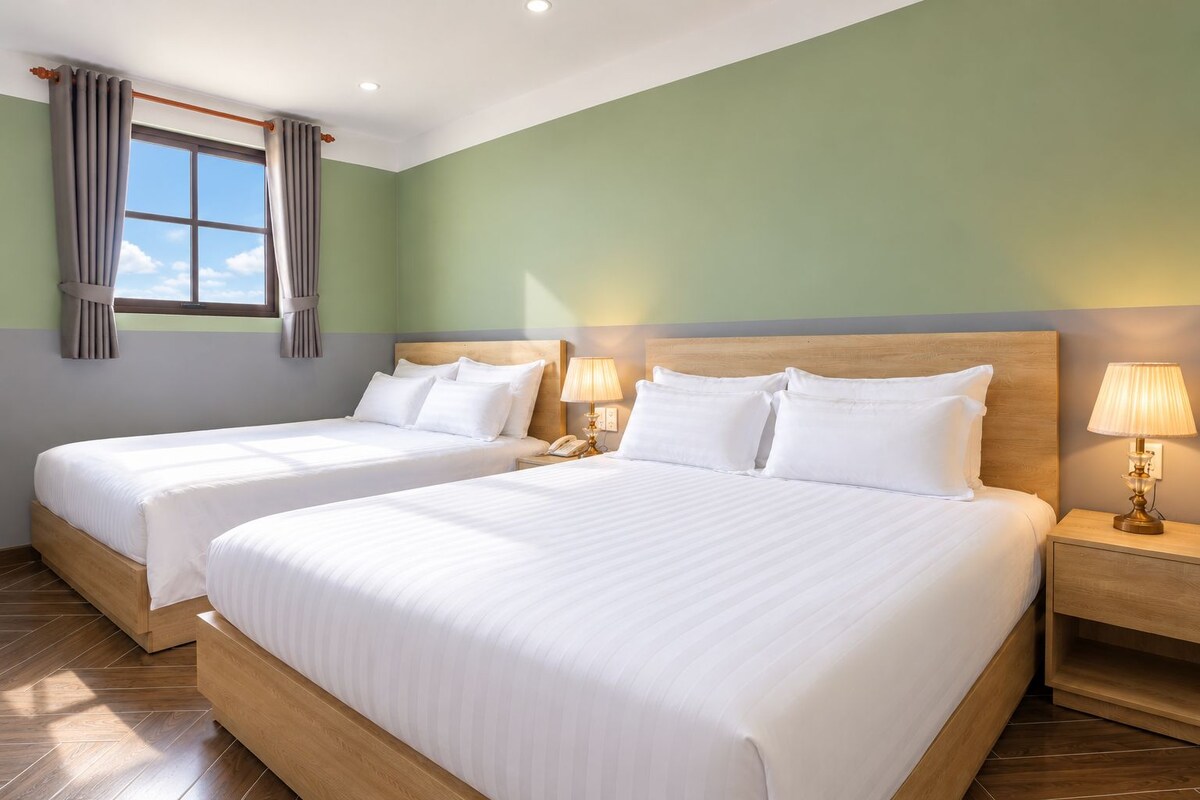 Quarto de hotel com duas camas, uma janela com cortinas, luminárias de cabeceira e piso de madeira.