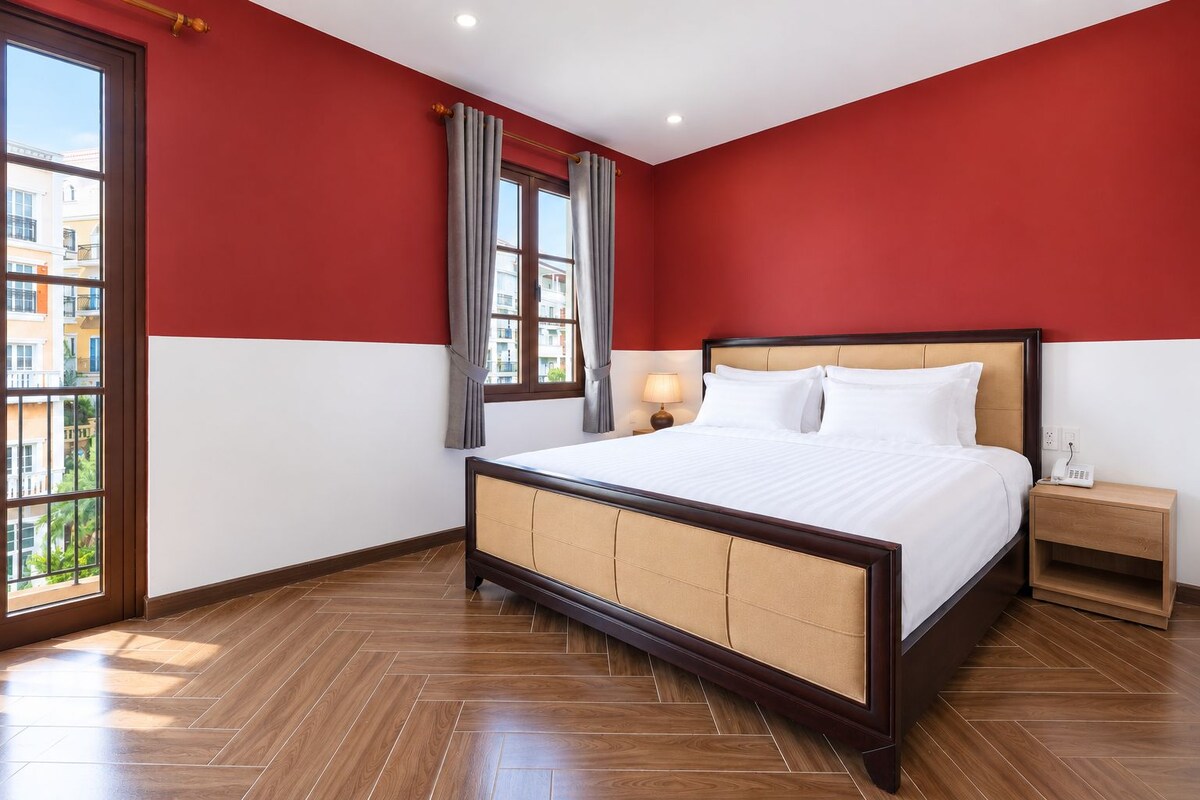 Quarto de hotel com uma cama grande, mesa de cabeceira, abajur e janela com cortinas.