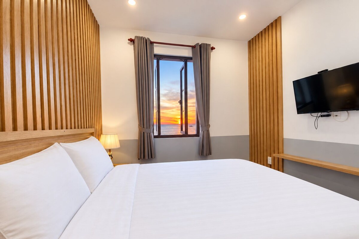 Quarto de hotel com cama, televisão presa na parede e janela com cortinas.