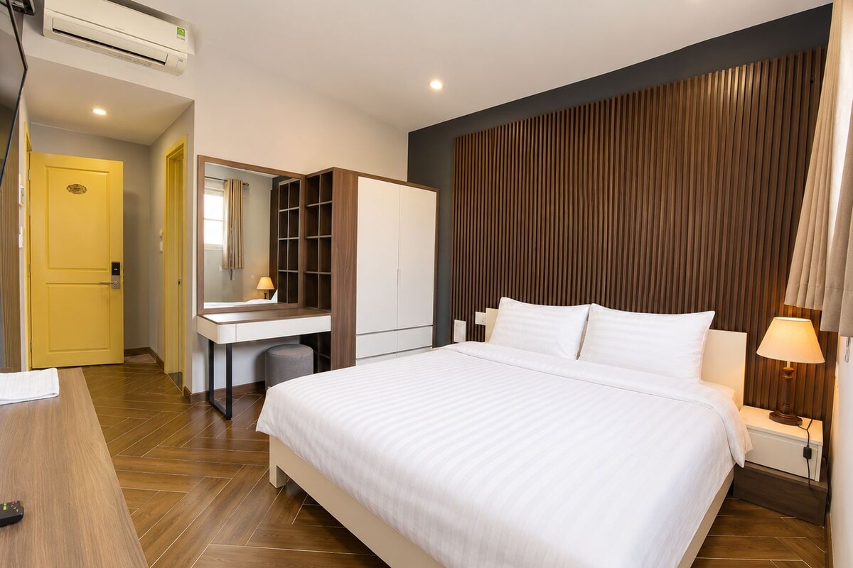 Quarto de hotel com cama, escrivaninha, espelho e guarda-roupa.