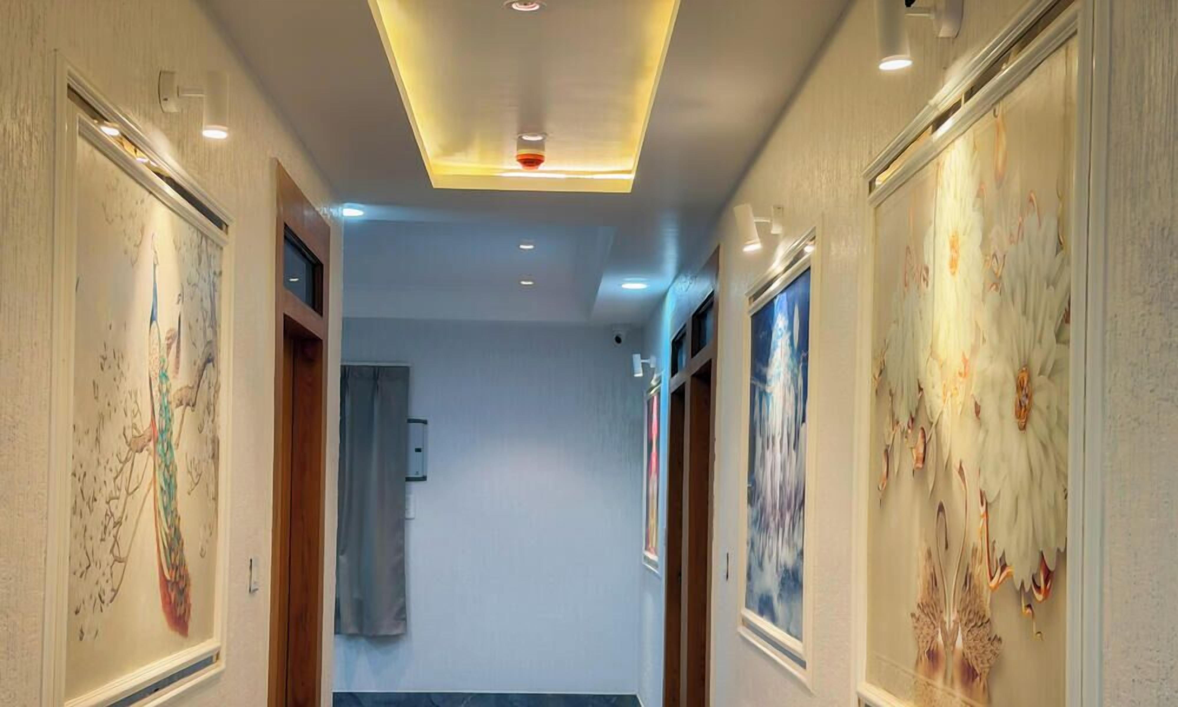 Um corredor com obras de arte emolduradas nas paredes, iluminação embutida no teto e uma porta no final.