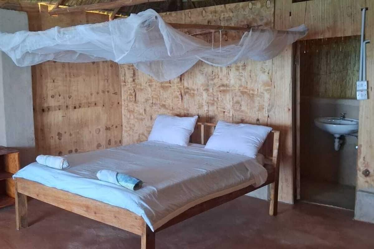 Uma cama de madeira com lençóis brancos, uma mesa de cabeceira e uma mosquiteira pendurada.