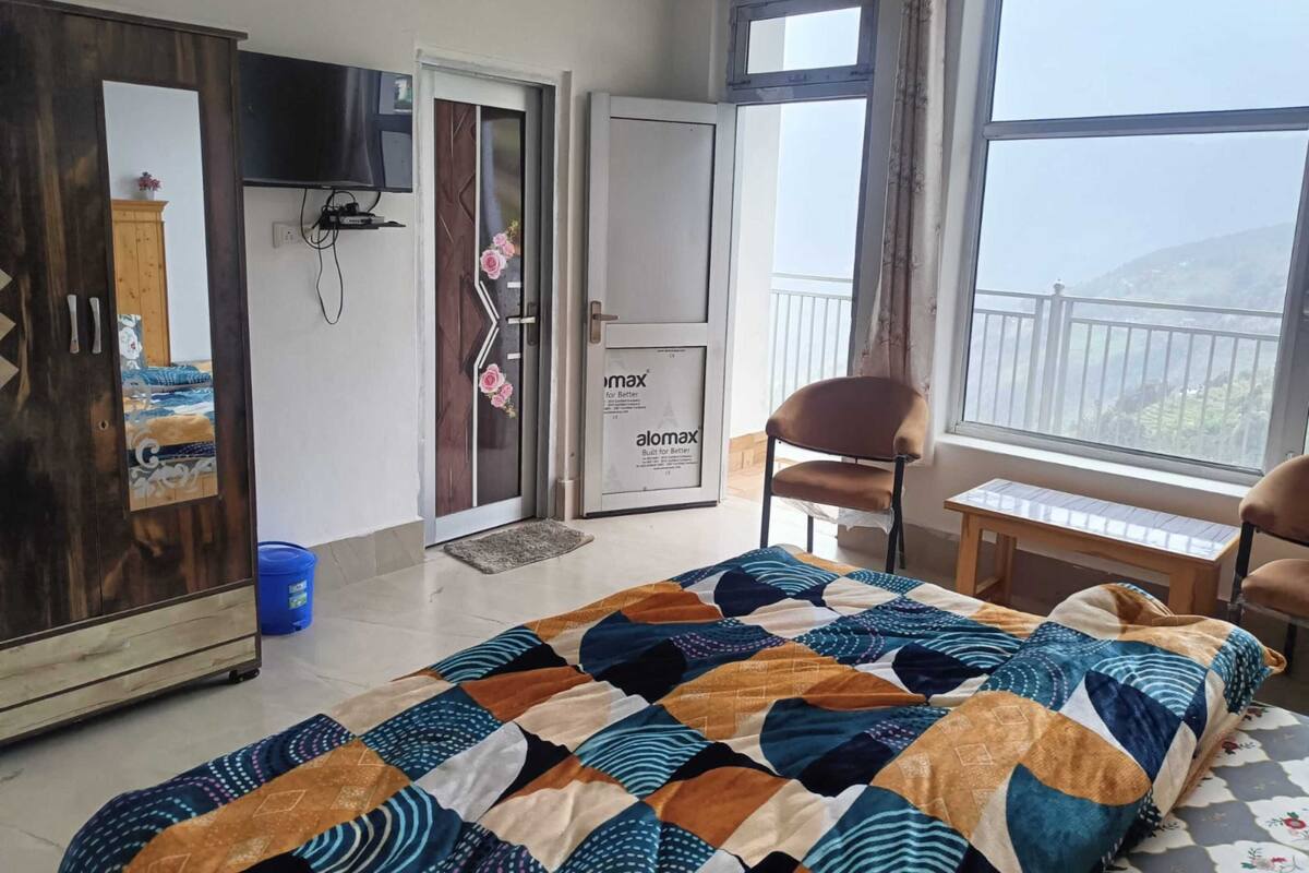 Quarto com cama, guarda-roupa, televisão, escrivaninha e varanda com vista.