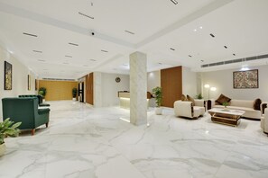 Um hall amplo com piso de mármore, área de estar com sofás e poltronas, e um balcão de recepção.