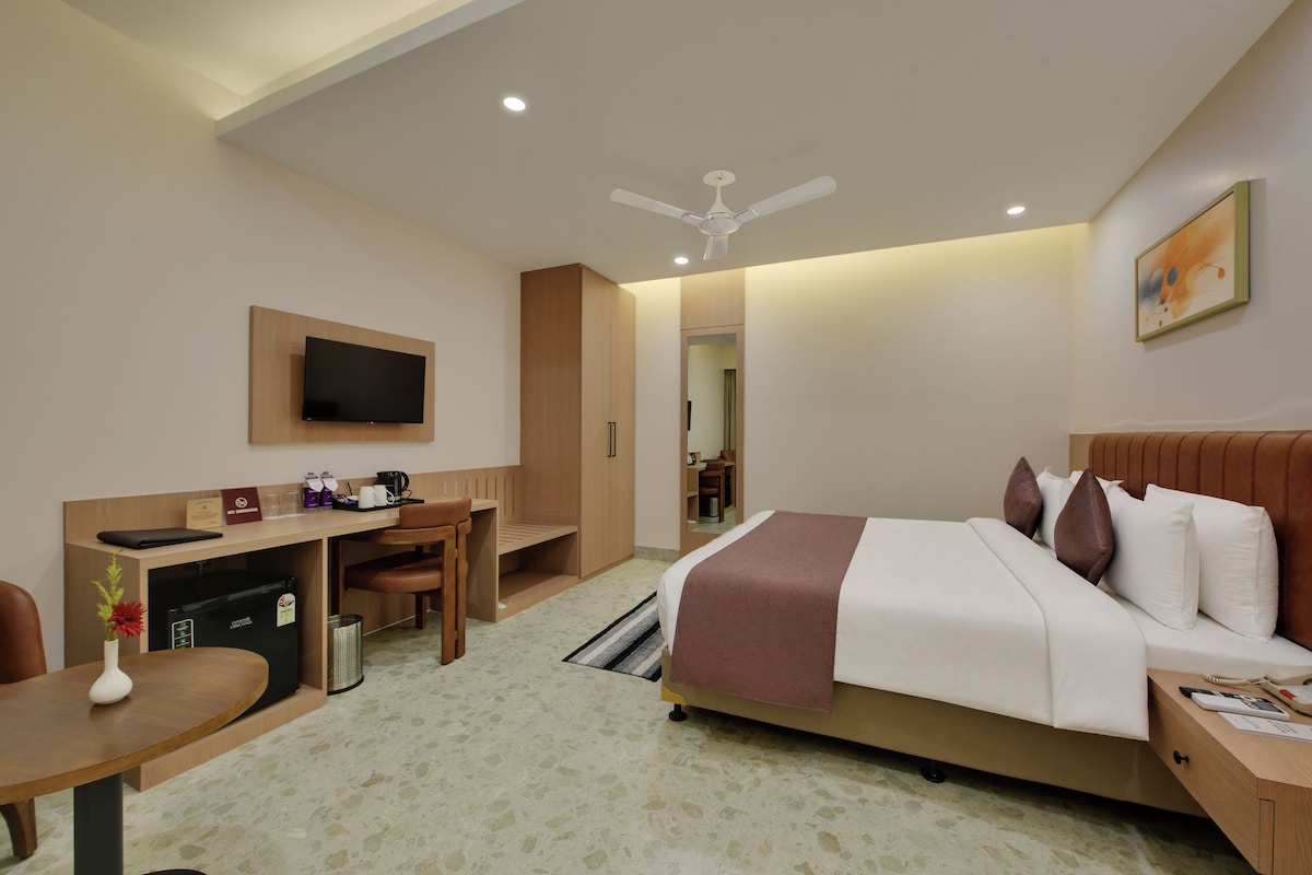 Quarto de hotel com cama, escrivaninha, cadeira, televisão e ventoinha no teto.