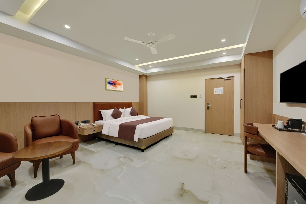 Quarto de hotel com cama, escrivaninha, cadeira, televisão e ventoinha no teto.
