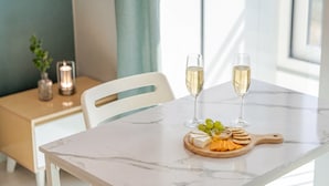 Uma mesa de mármore com duas taças de champanhe, uma tábua de madeira com queijo e uvas, e uma cadeira branca.