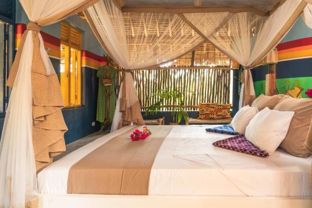 Quarto com cama, dossel, janela com cortinas e vista para o exterior.