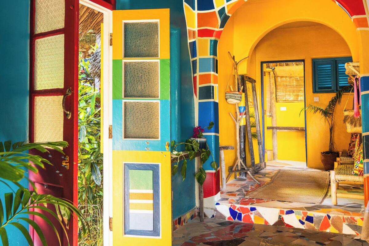 Um corredor colorido com piso de azulejos, porta vermelha e parede amarela.