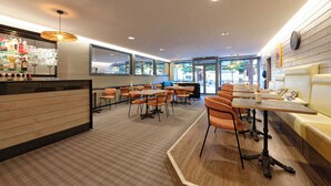 Um restaurante com área de bar, várias mesas e cadeiras, e vista através de grandes janelas.