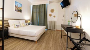 Quarto de hotel com cama, mesa de cabeceira, abajur, televisão e escrivaninha com cadeira.