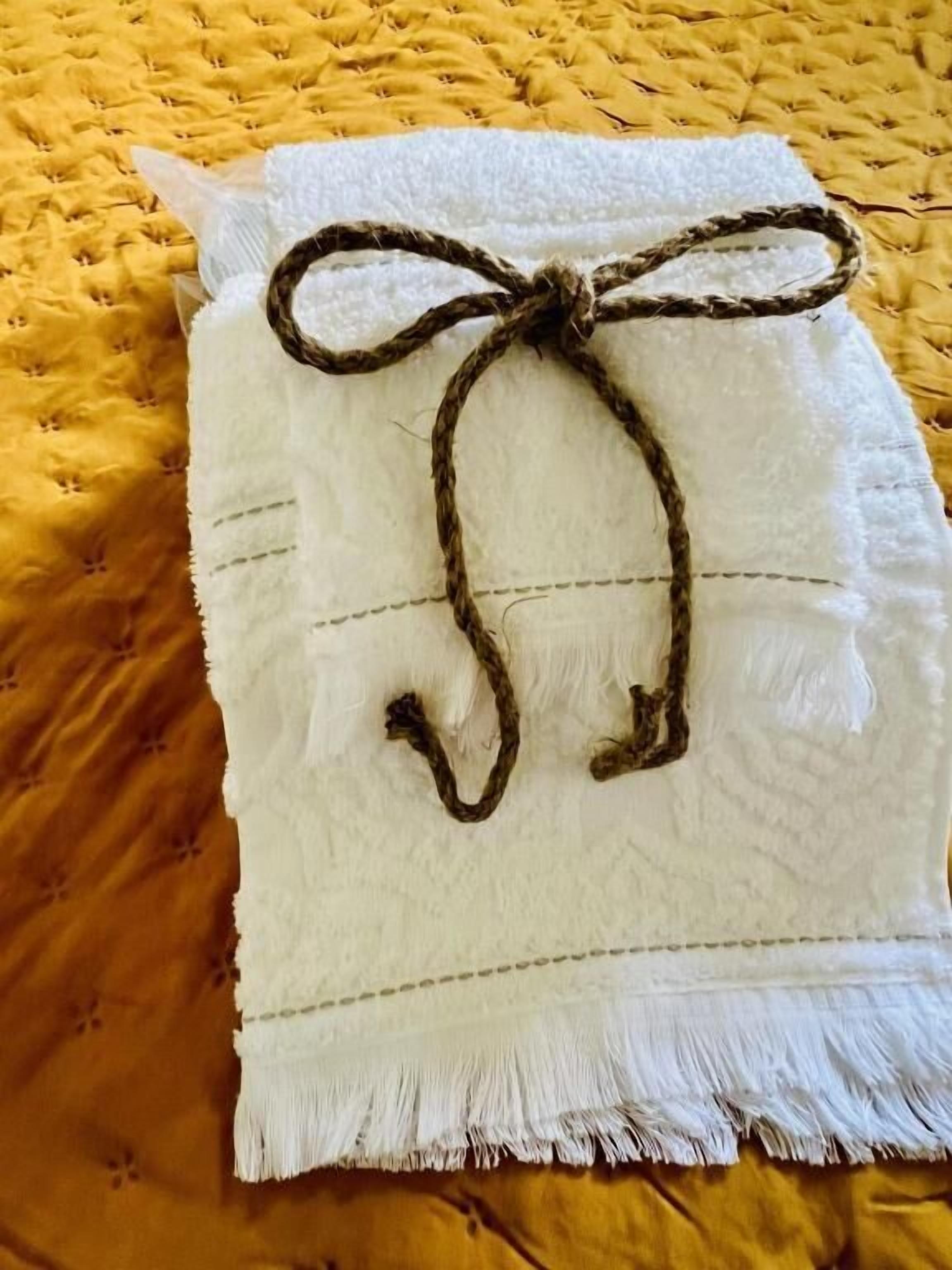 Toalha branca com um cordão trançado amarrado em laço, sobre uma superfície amarela texturizada.