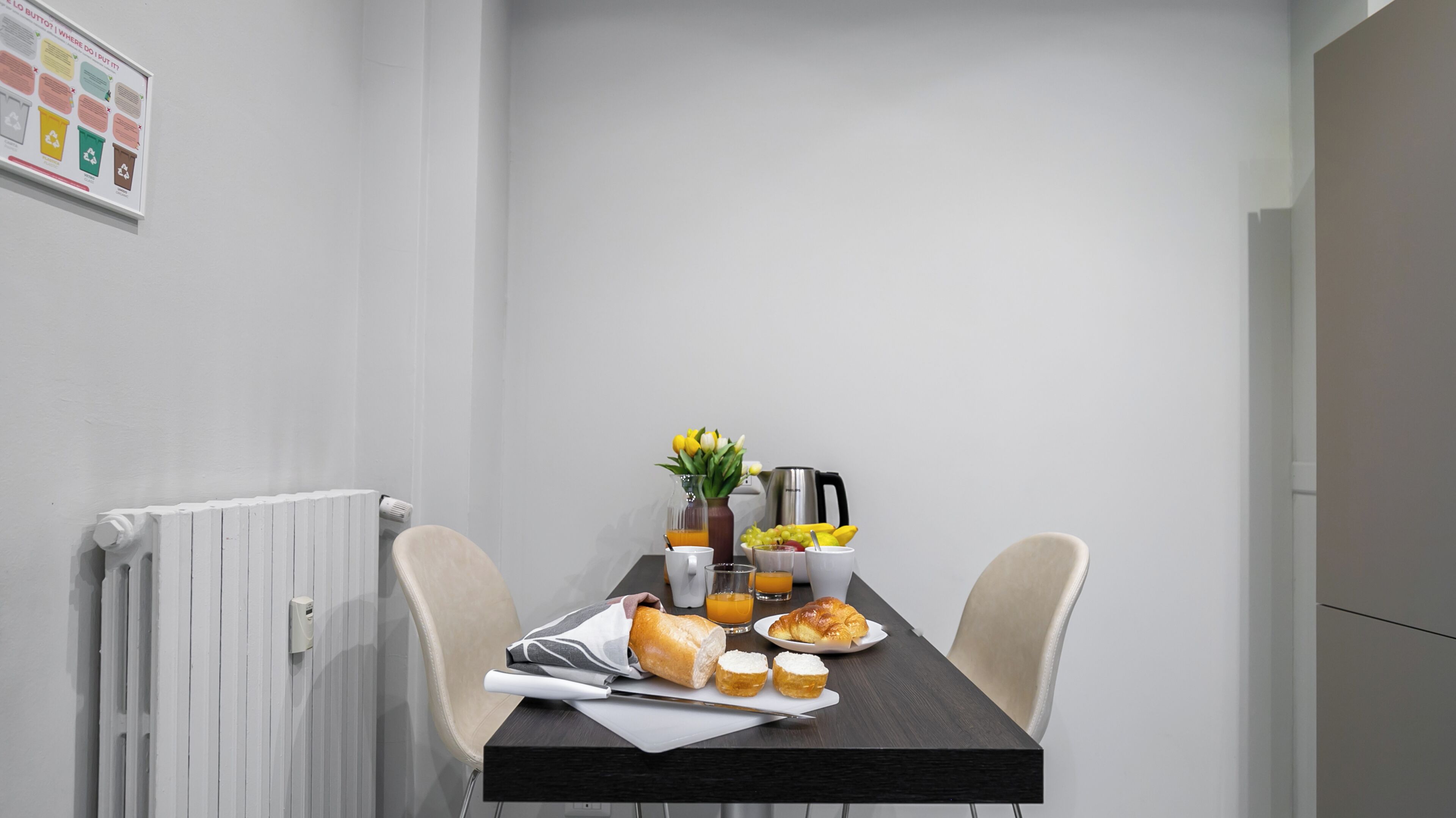 Uma sala de jantar moderna com uma mesa posta para o café da manhã, incluindo pão, doces, frutas e uma cafeteira.