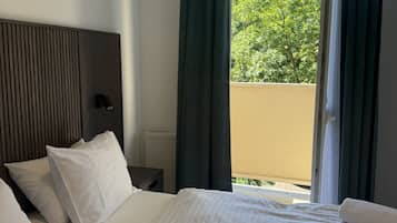 Quarto de hotel com cama, mesa de cabeceira, luminária e vista para o verde lá fora.