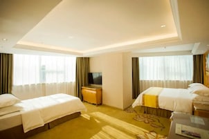 Quarto de hotel com duas camas, televisão, escrivaninha e uma janela grande com cortinas.
