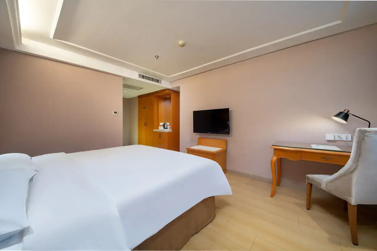 Quarto de hotel com cama, escrivaninha, cadeira, televisão e armário.