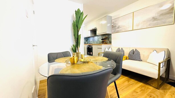 Um espaço de estar moderno com área de jantar, mesa e cadeiras de vidro, sofá com almofadas estampadas e cozinha ao fundo.