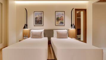 Quarto de hotel com duas camas individuais, piso de madeira, tapete, duas luminárias fixadas na parede e duas imagens emolduradas.