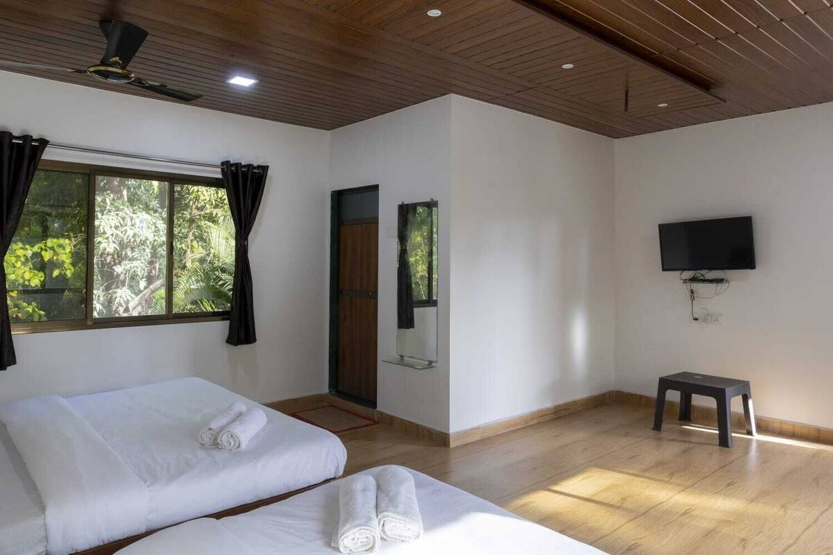 Quarto com duas camas, televisão, ventoinha no teto e janela com cortinas.
