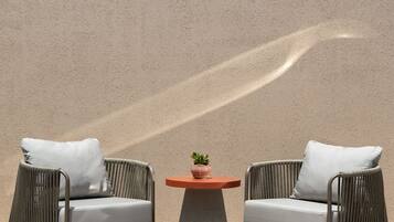 Uma área de estar externa com duas cadeiras de vime, uma mesa redonda e um vaso com planta.
