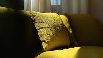 Uma cama com manta e almofadas amarelas, uma janela com cortinas e vista para o céu.